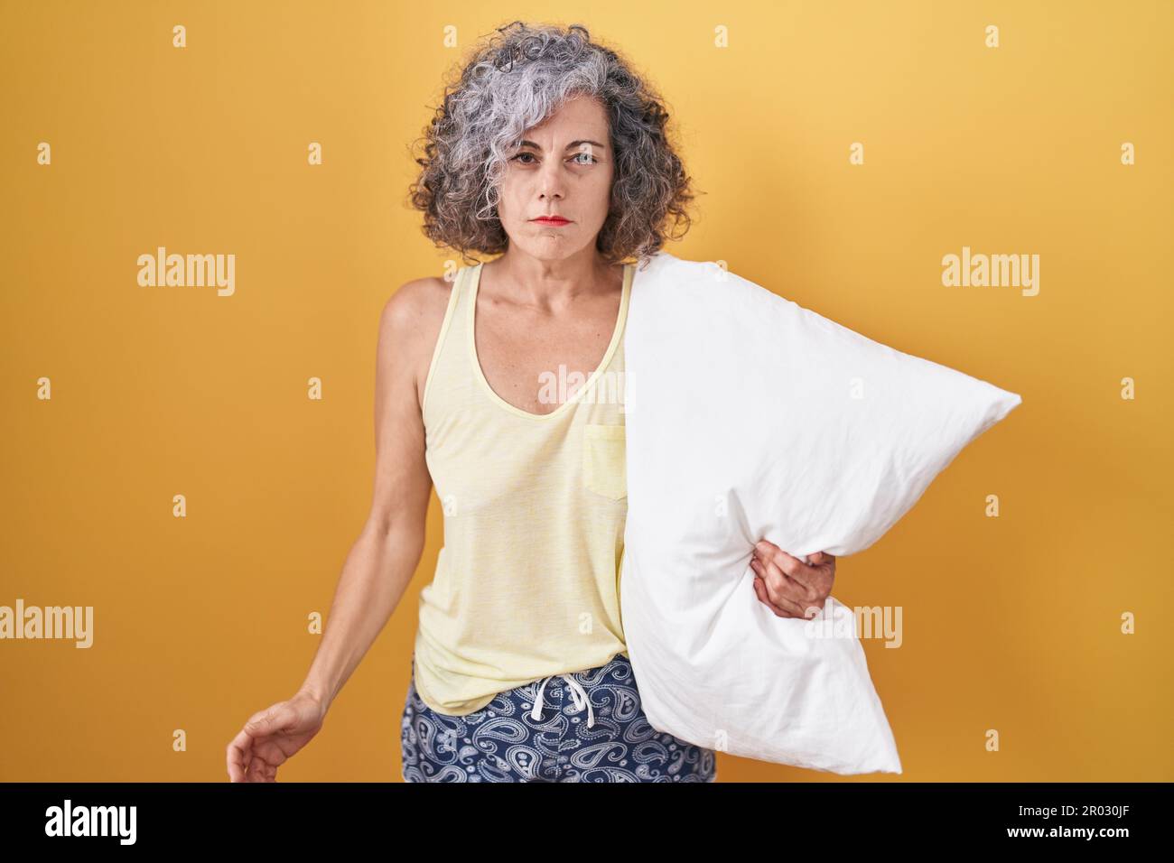 Middle age woman with grey hair wearing pijama hugging pillow depressed ...