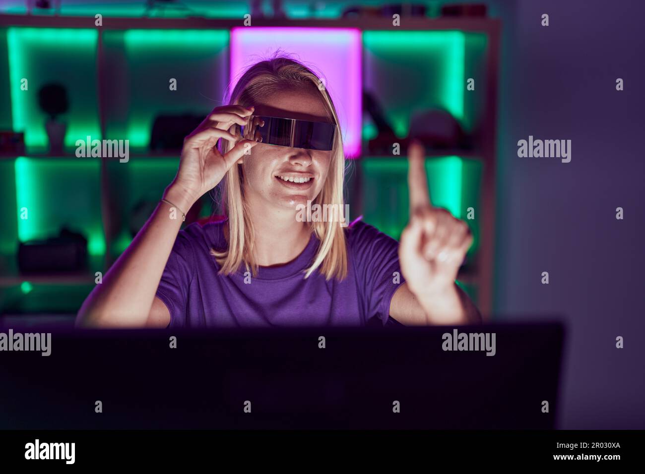 Young blonde woman streamer using virtual reality glasses at gaming ...