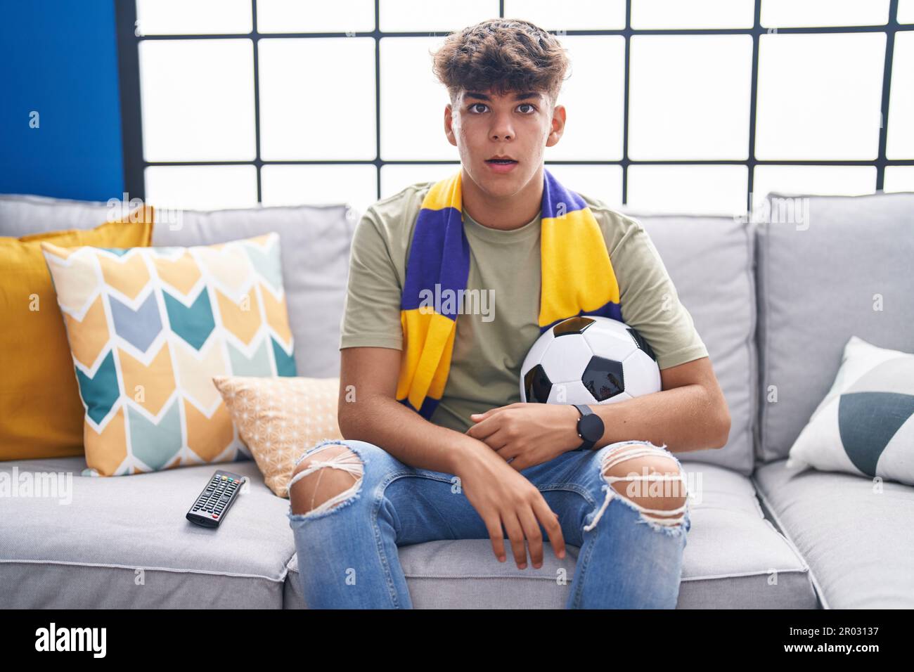 Hispanic teenager sitting on the sofa watching football match scared ...