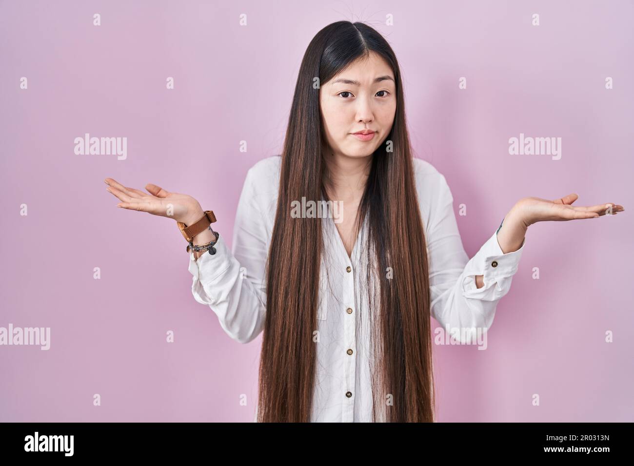 Chinese young woman standing over pink background clueless and confused ...