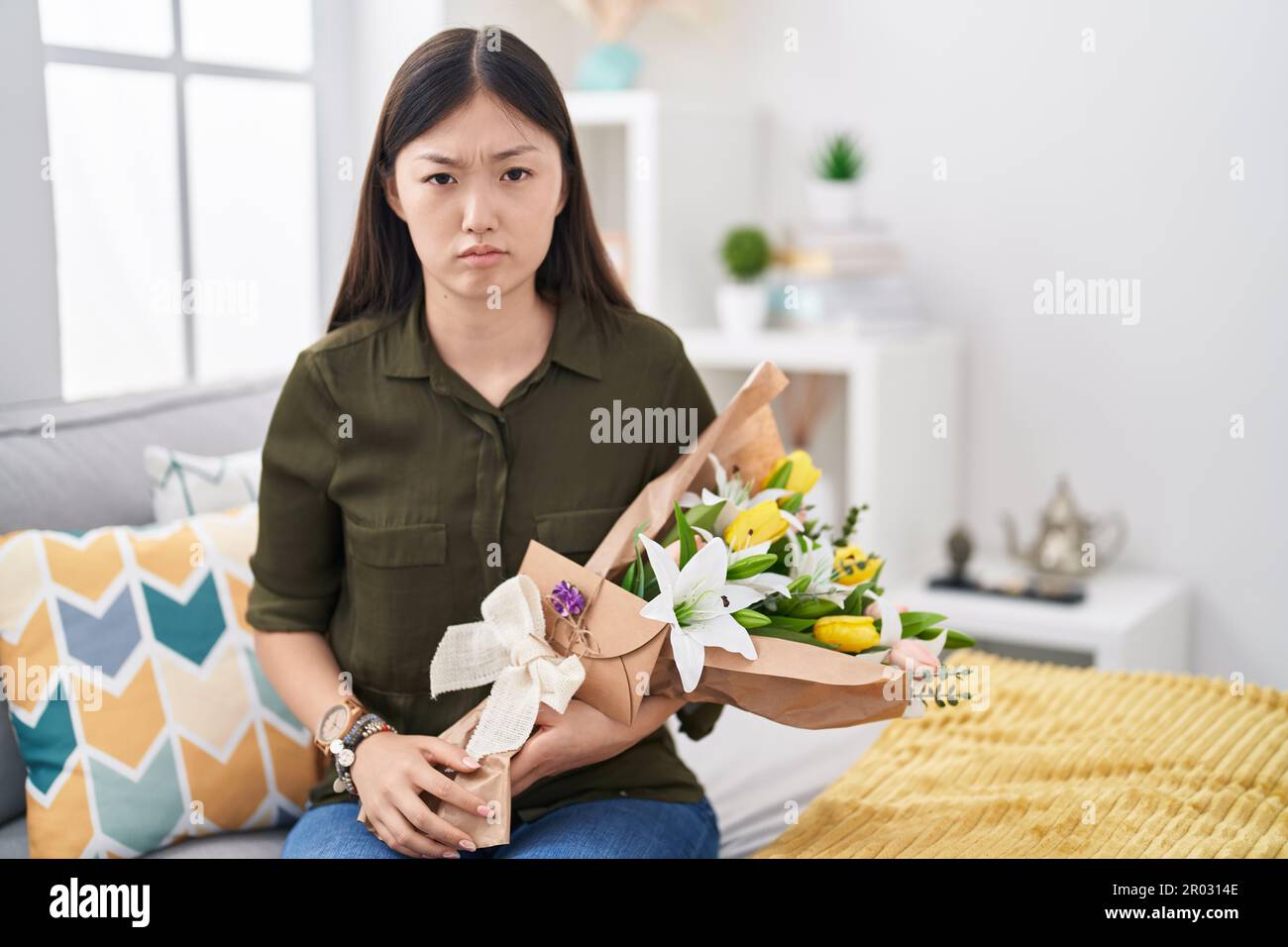 Chinese young woman holding bouquet of white flowers depressed and ...