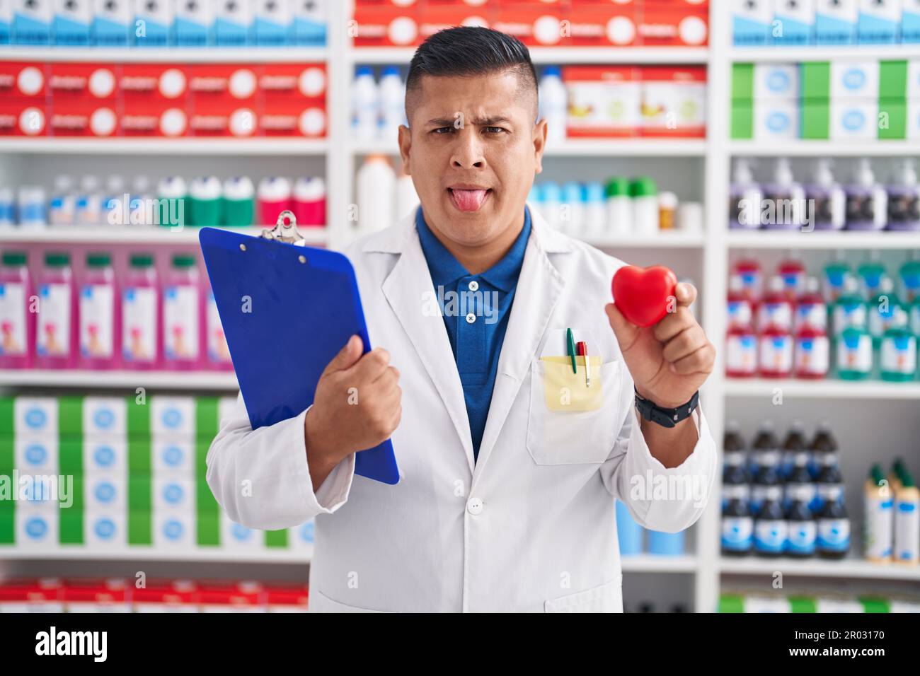 Young hispanic man working at pharmacy drugstore holding heart sticking ...