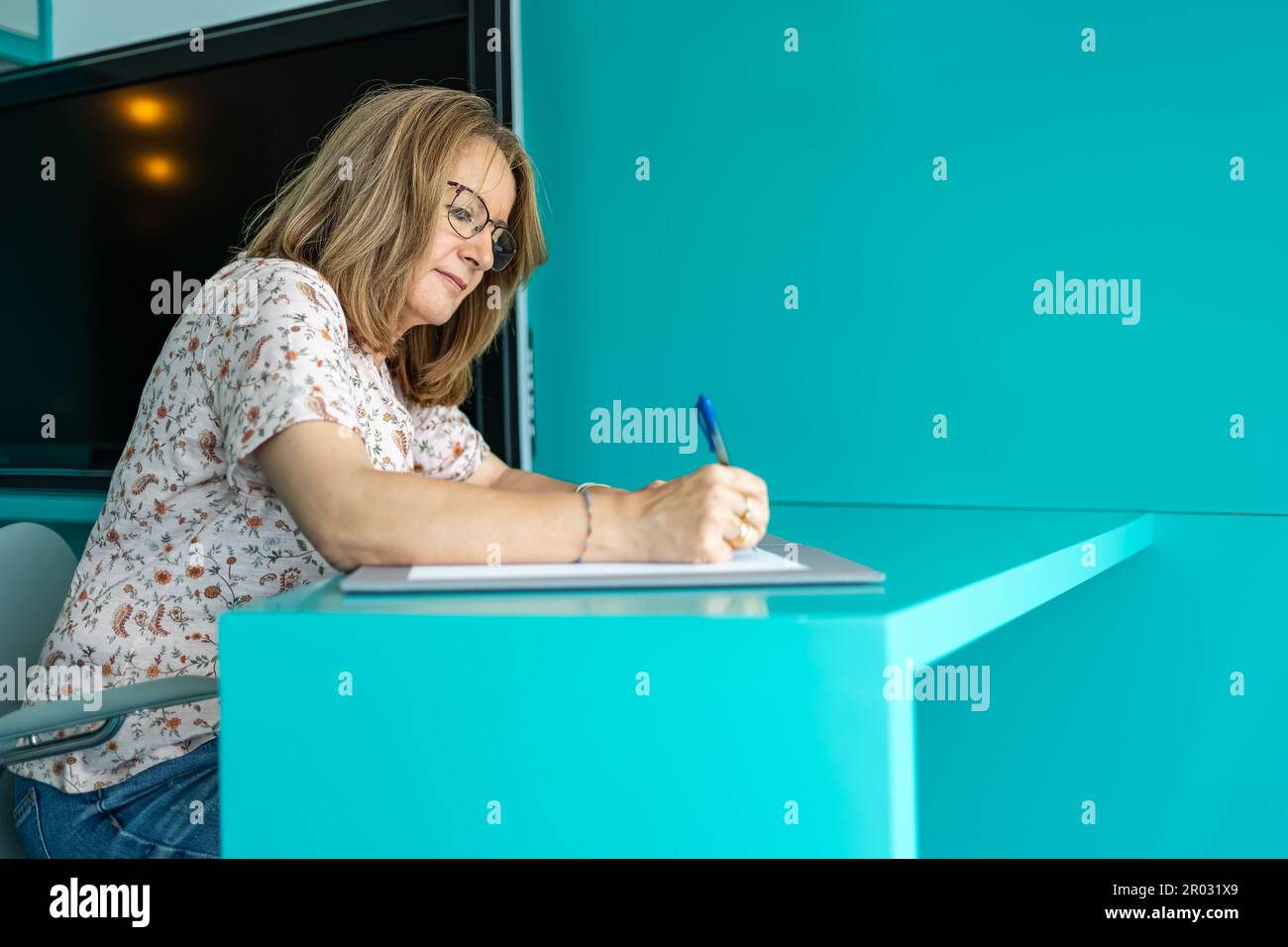 Woman writing at a modern table next to a large window overlooking the ...