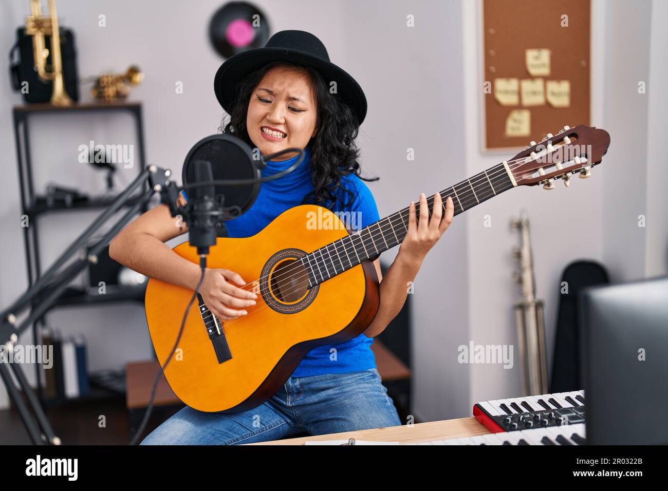 Young chinese woman artist singing song playing guitar at music studio ...