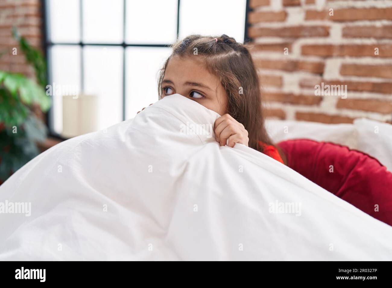 Adorable hispanic girl sitting on the bed with fear expression at ...