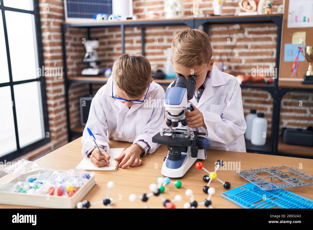 Adorable boys students using microscope writing notes at laboratory ...