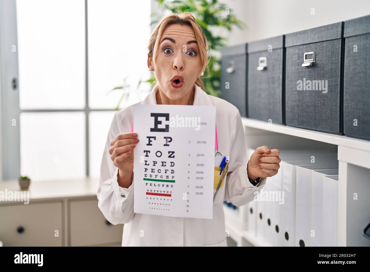 Hispanic optician woman holding medical exam scared and amazed with ...