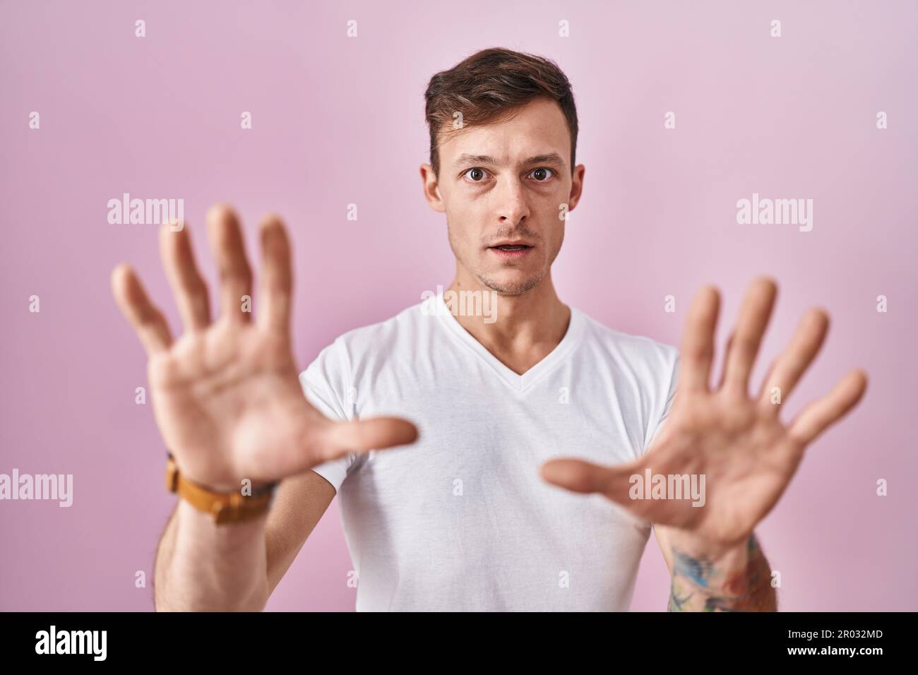 Caucasian man standing over pink background afraid and terrified with ...