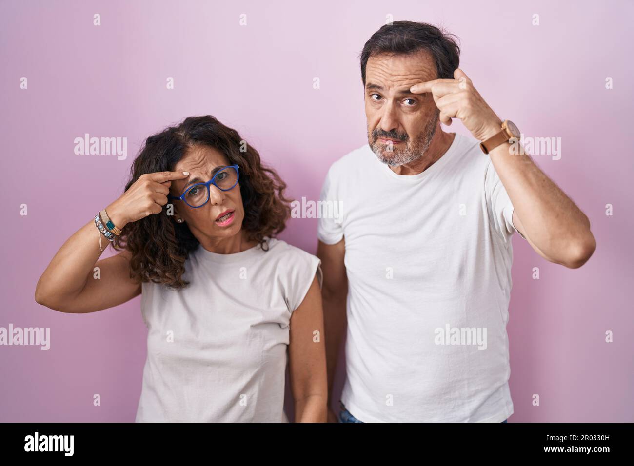 Middle age hispanic couple together over pink background pointing ...