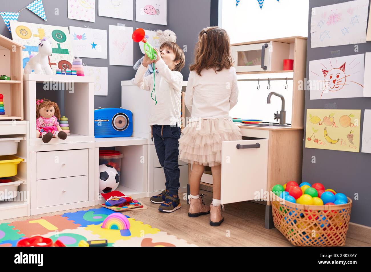 Adorable boy and girl playing with play kitchen using trumpet at ...