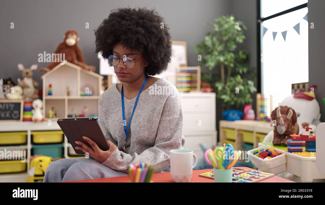 African american woman preschool teacher writing on touchpad at ...