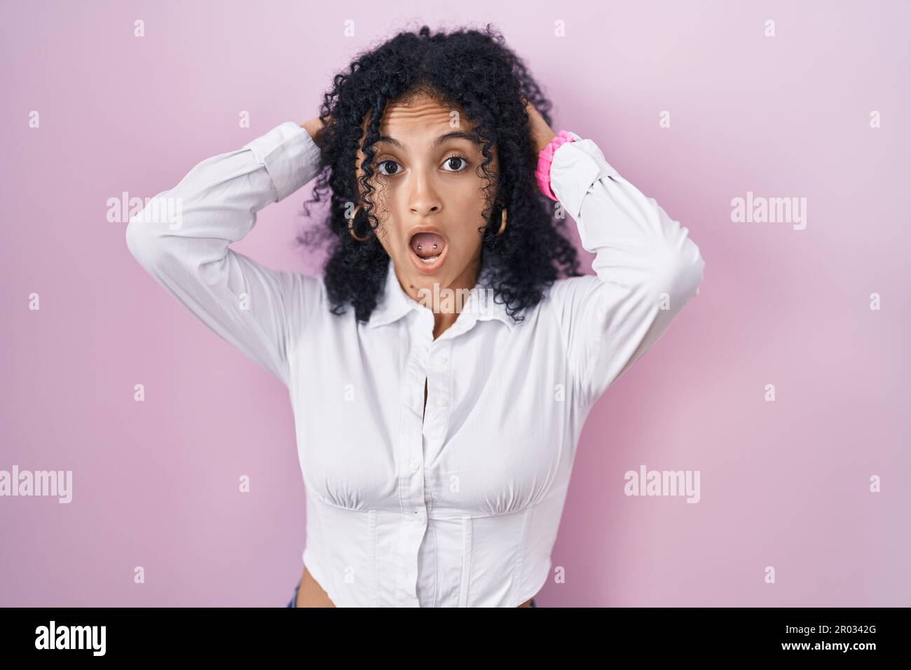 Hispanic woman with curly hair standing over pink background crazy and ...