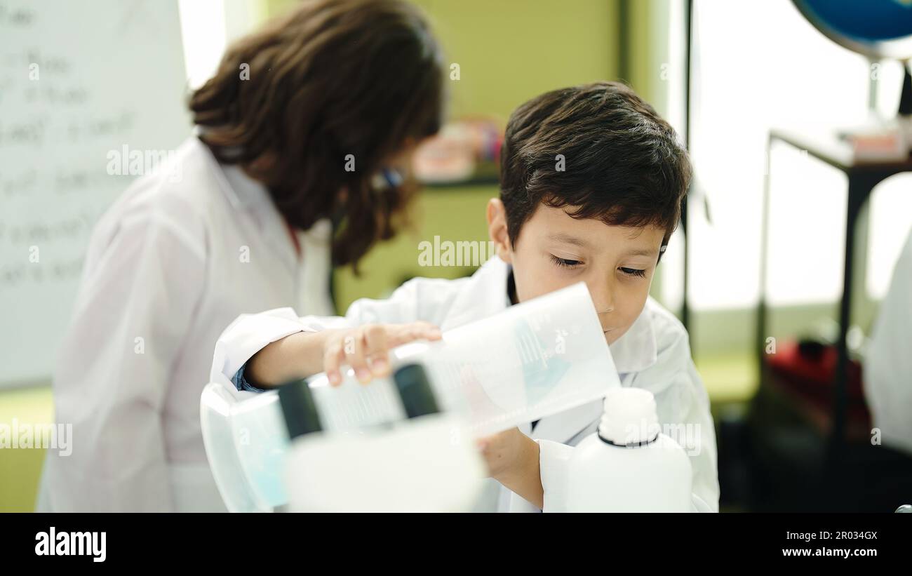 Adorable boy and girl student pouring liquid on test tube at laboratory ...
