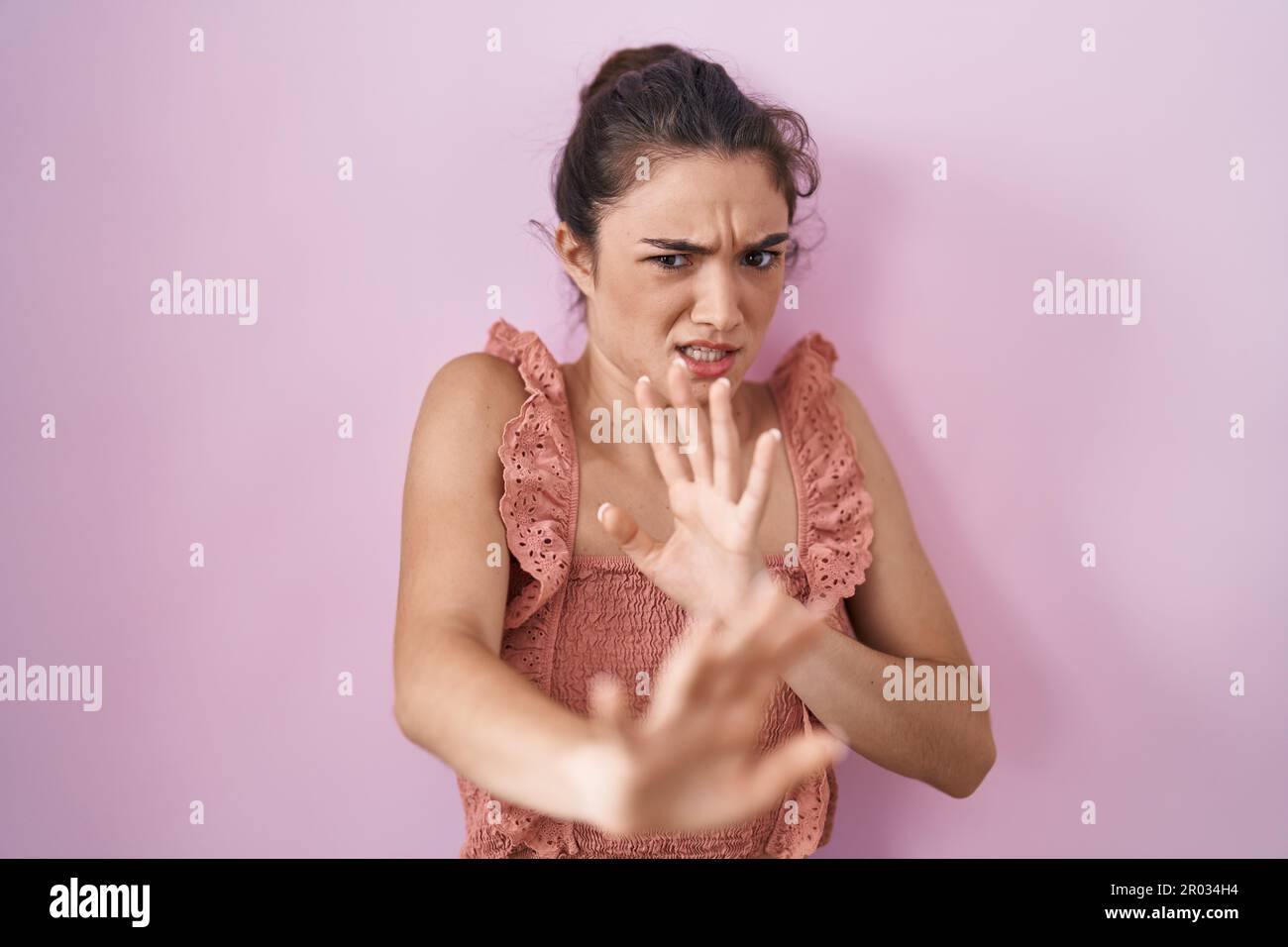 Young teenager girl standing over pink background disgusted expression ...