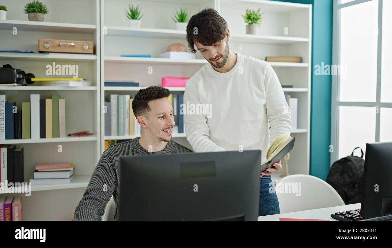Two men students using computer reading book studying at library university Stock Photo - Alamy