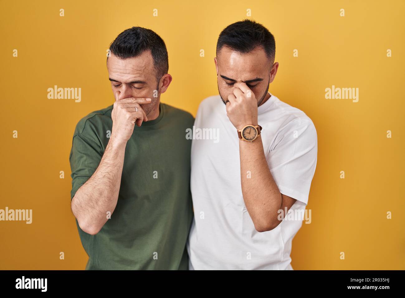 Homosexual couple standing over yellow background tired rubbing nose ...
