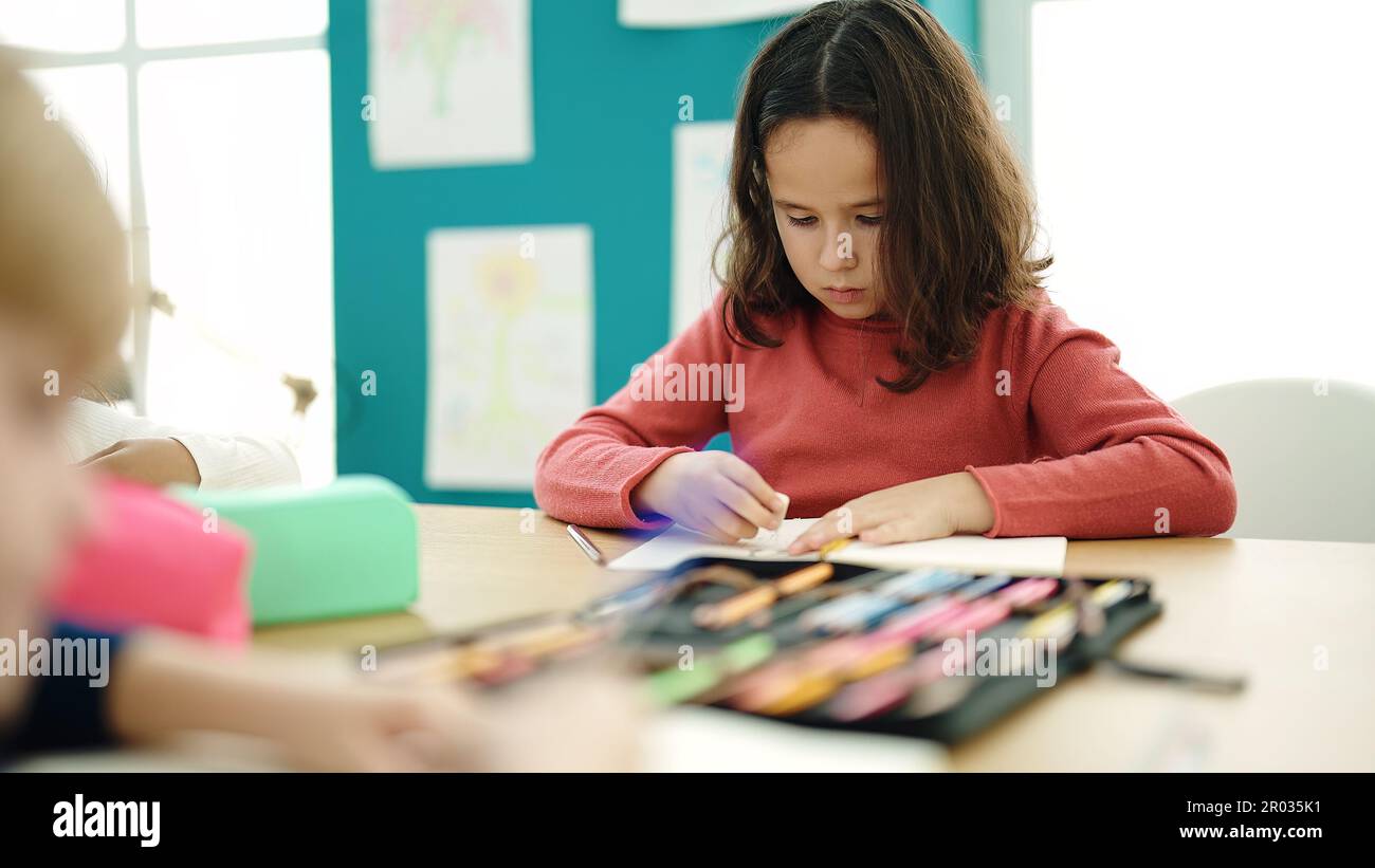 Adorable hispanic girl student writing on notebook at classroom Stock ...