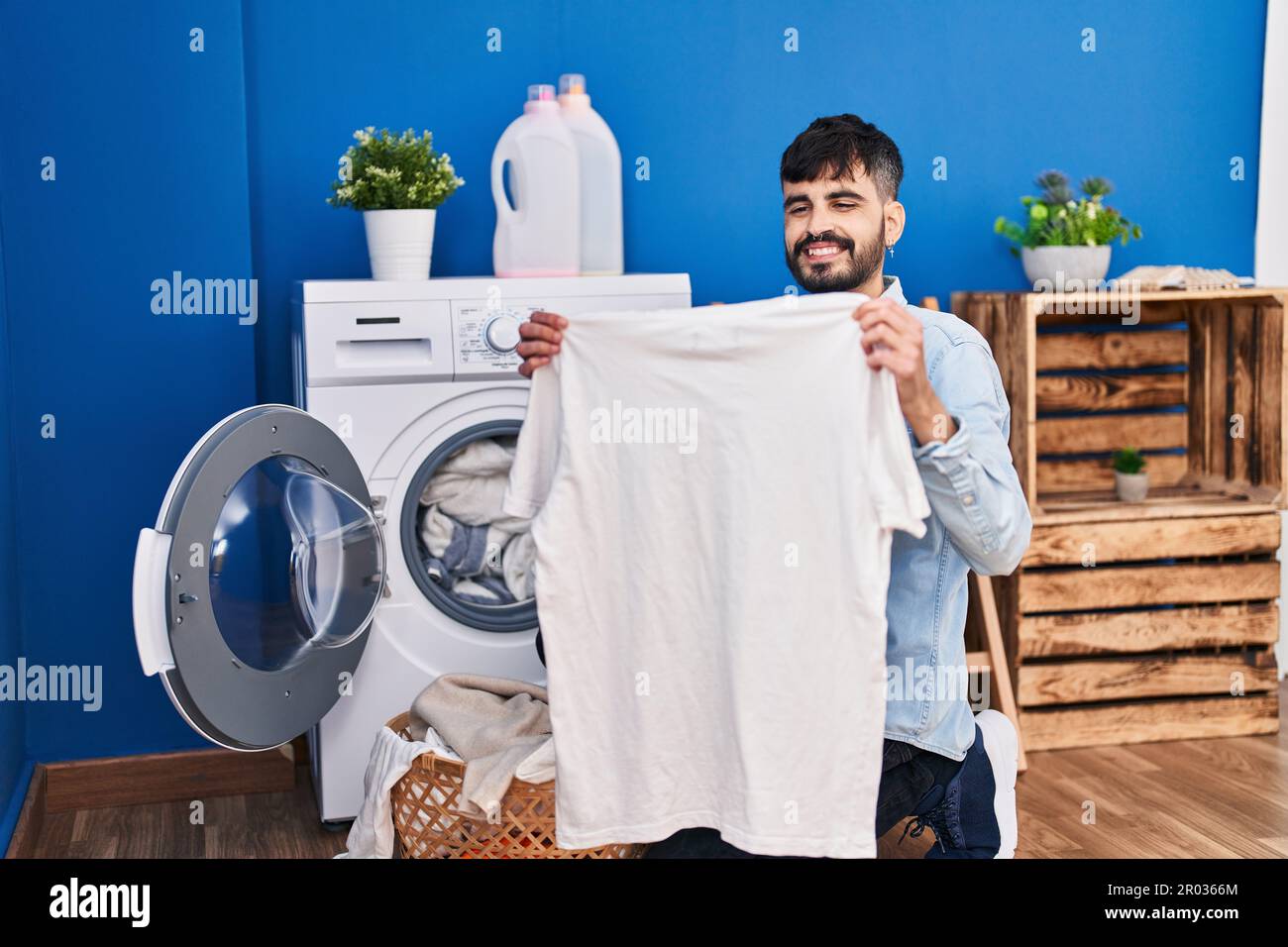 Young hispanic man holding white t shirt washing clothes at laundry ...