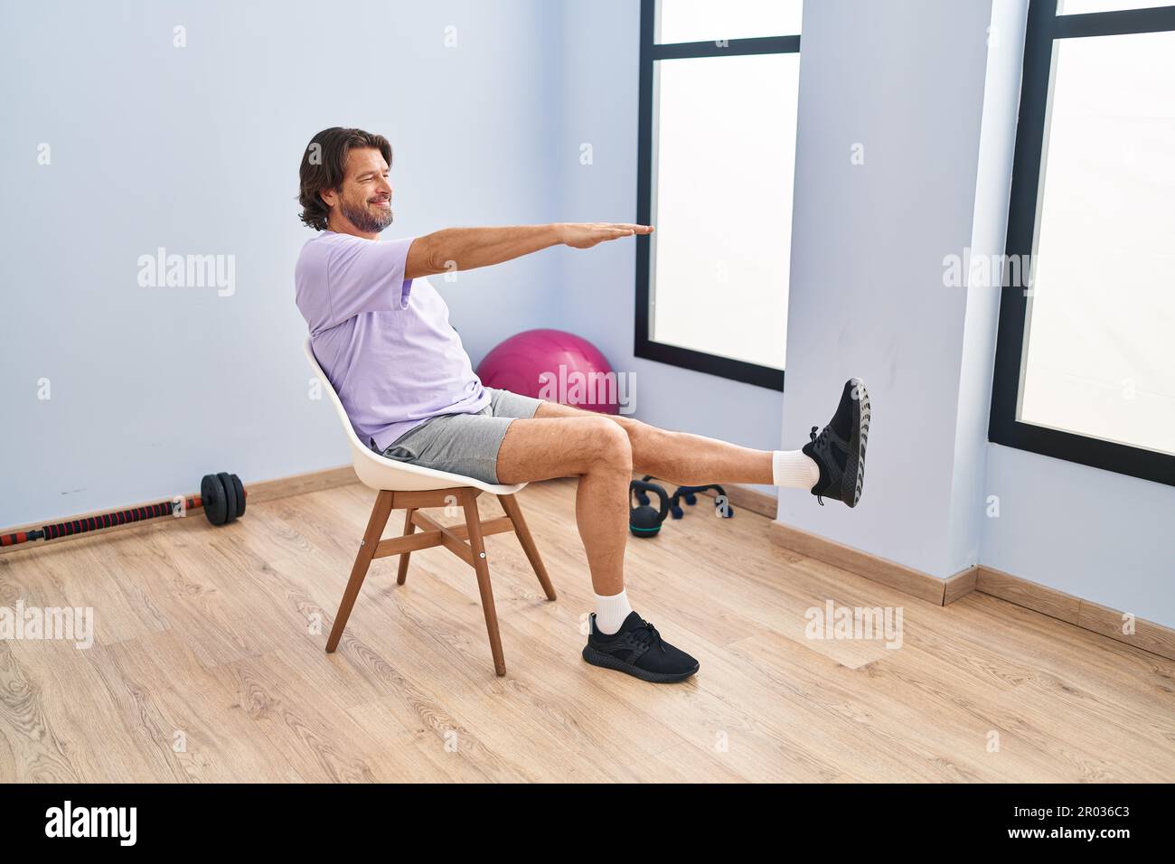 Middle age man smiling confident sitting on chair stretching at sport ...