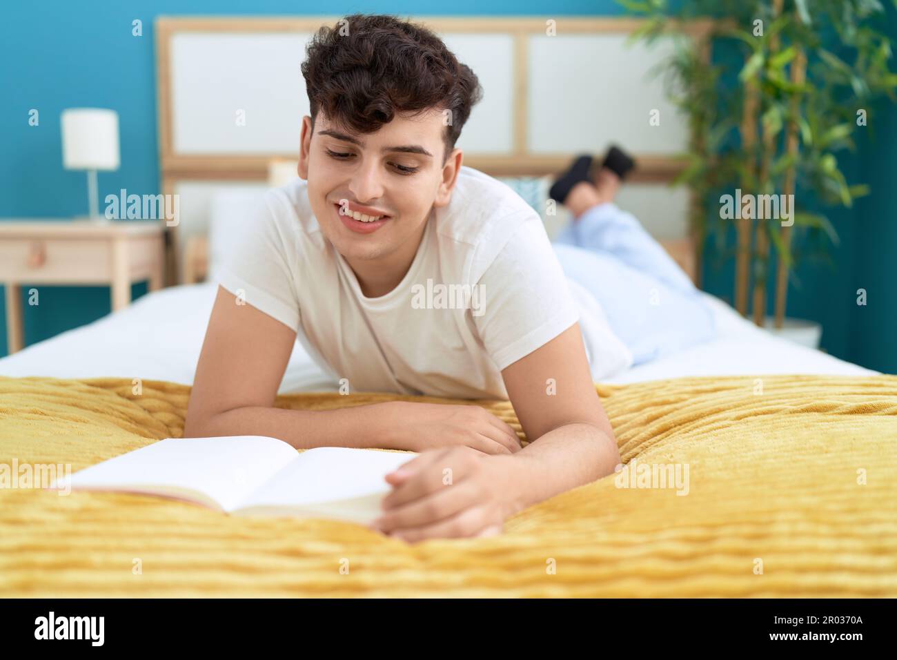 Non binary man reading book lying on bed at bedroom Stock Photo - Alamy