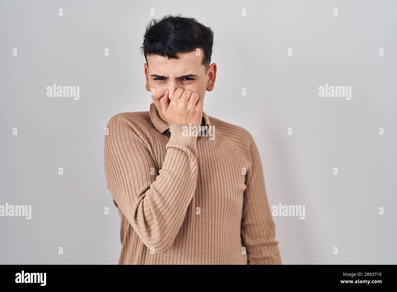Non binary person standing over isolated background smelling something ...