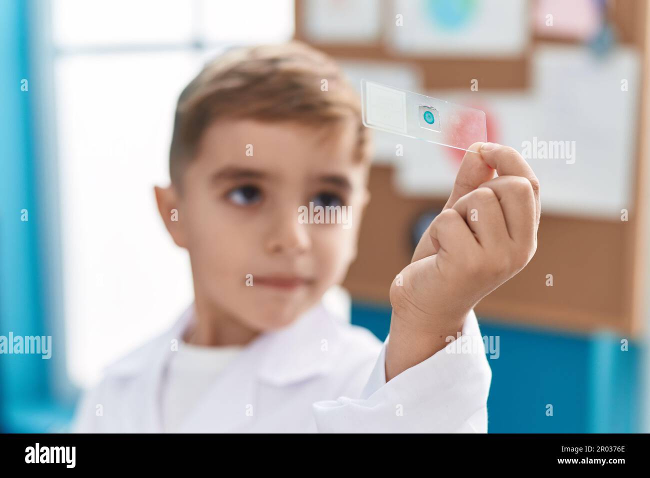 Adorable hispanic boy student looking sample at laboratory classroom ...