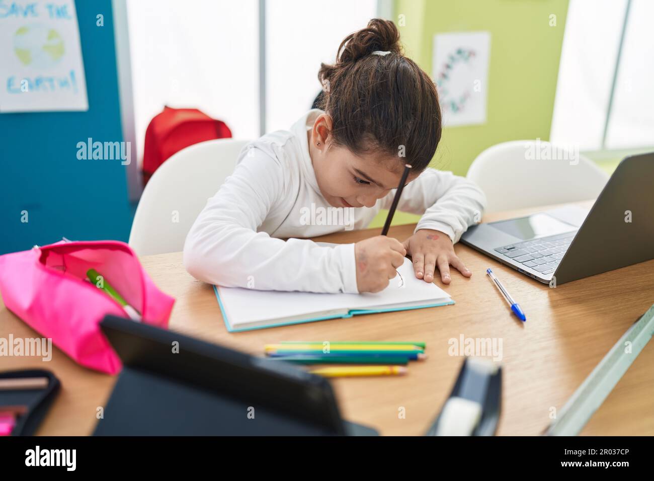 Adorable hispanic girl student writing on notebook at classroom Stock ...