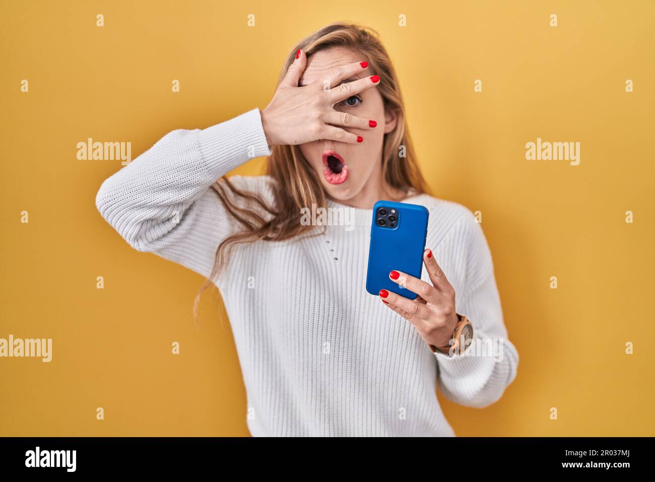 Young blonde woman using smartphone typing message peeking in shock ...