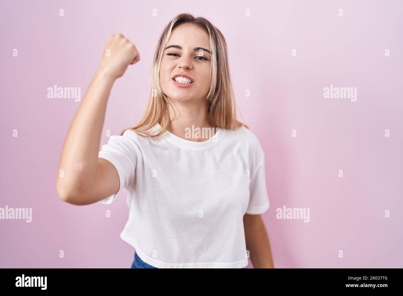 Young blonde woman standing over pink background angry and mad raising ...