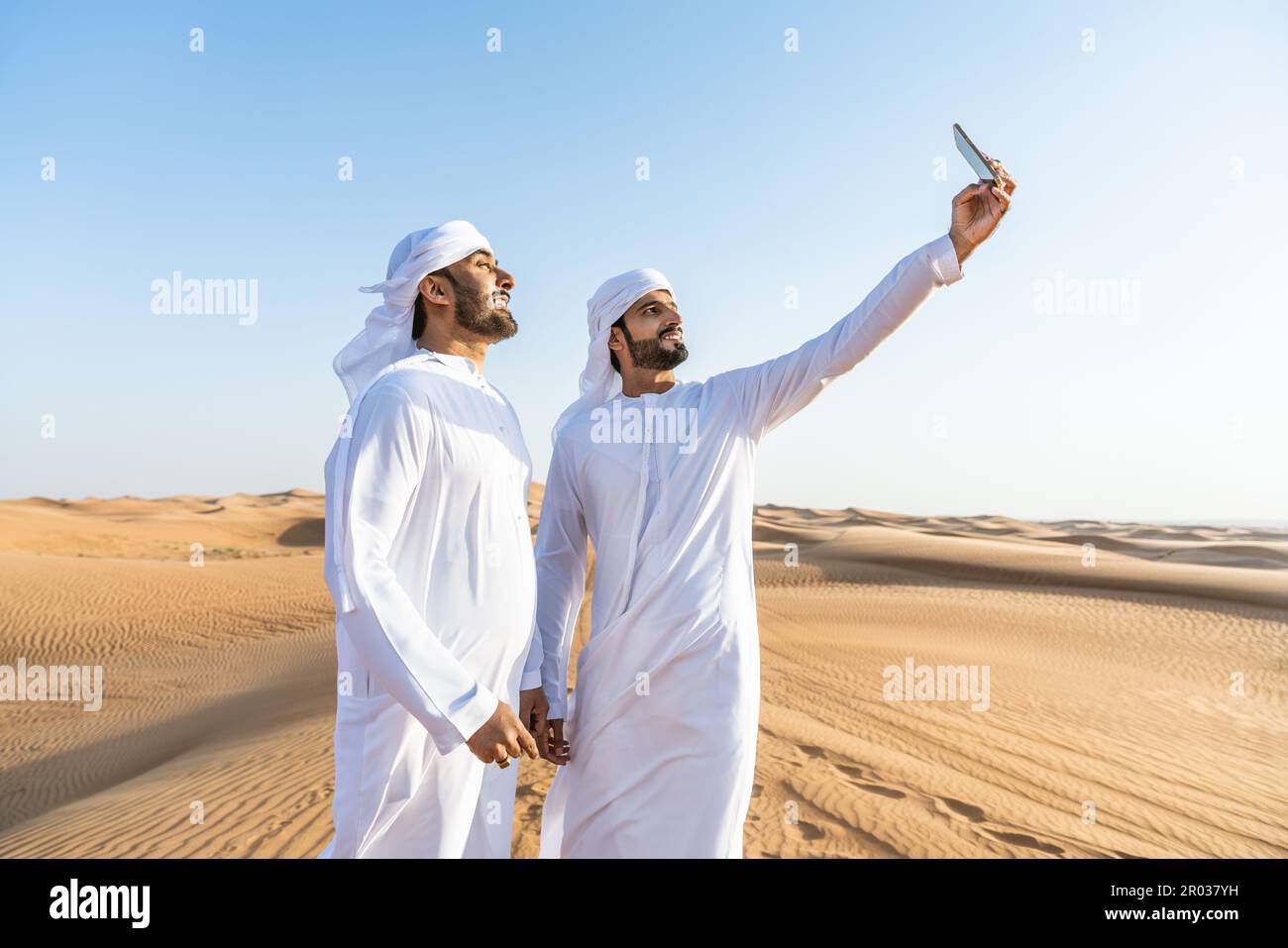 Two middle-eastern men wearing traditional emirati arab kandura bonding ...