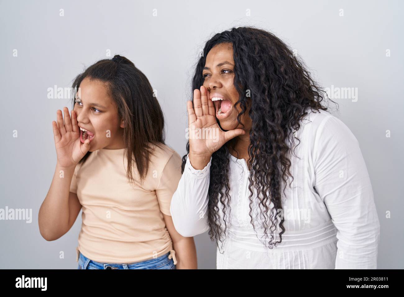 Mother and young daughter standing over white background shouting and ...