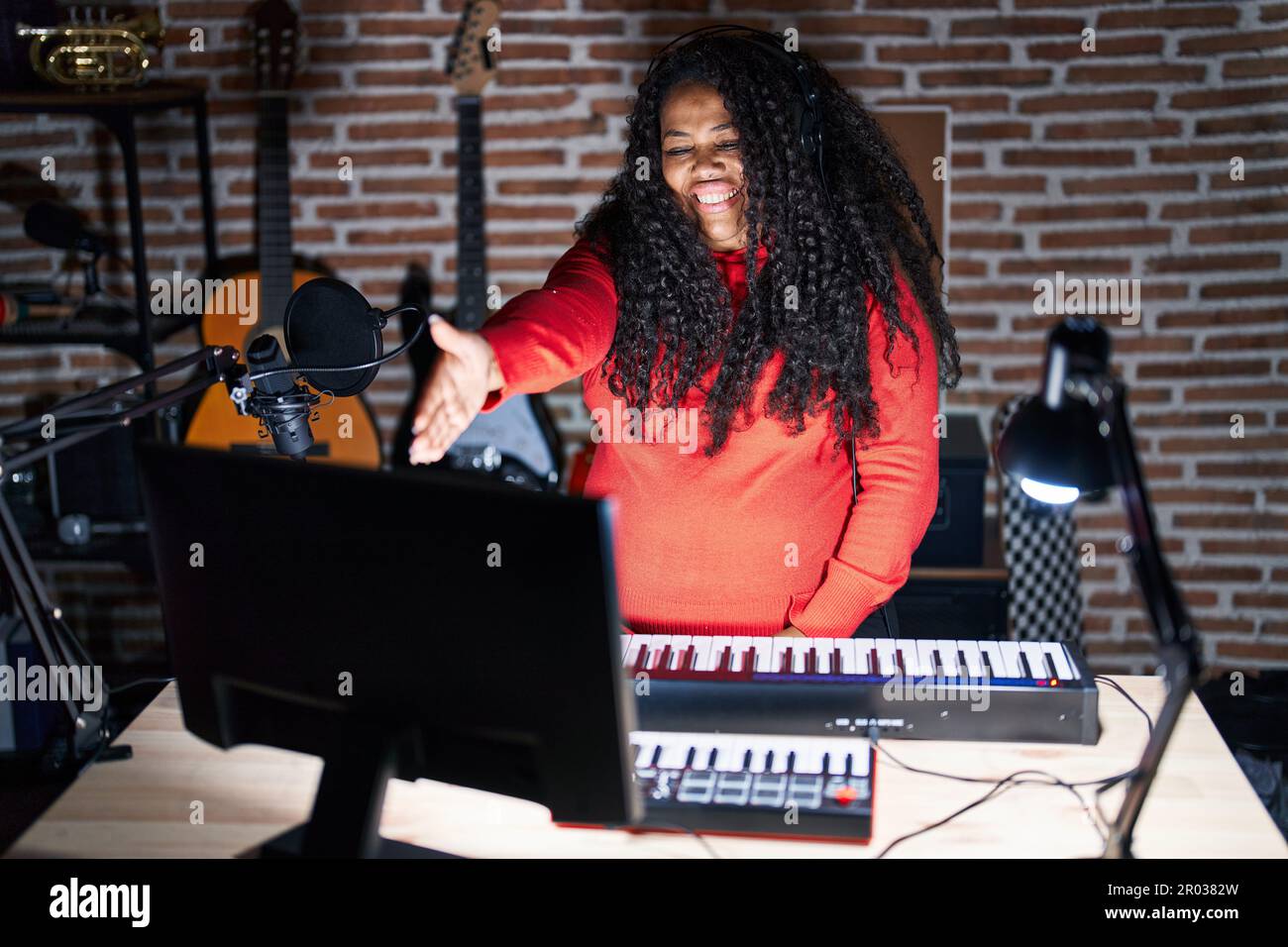 Plus size hispanic woman playing piano at music studio smiling friendly ...