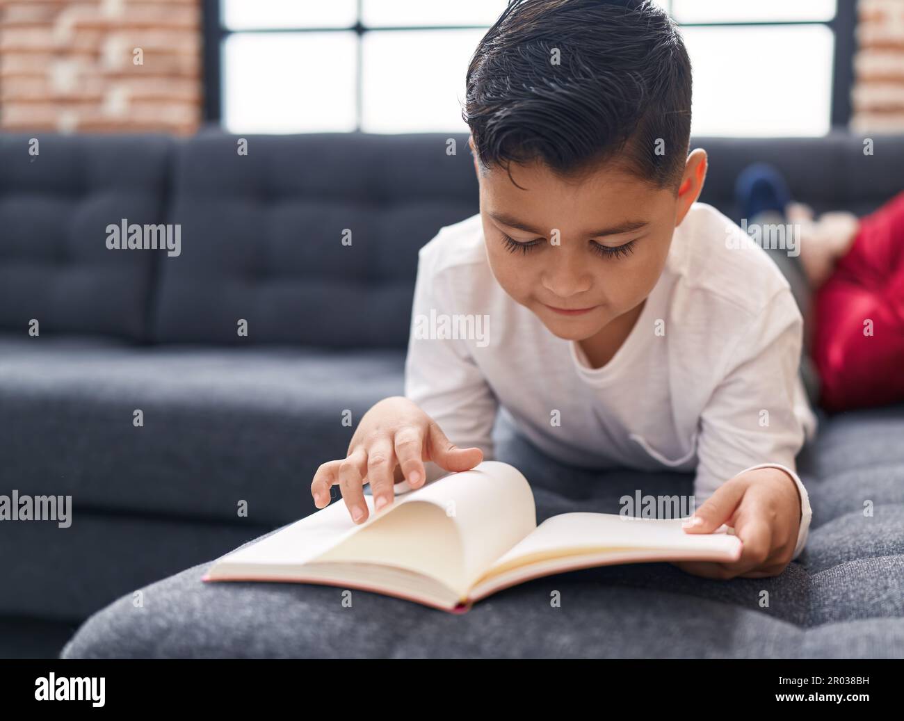 Adorable hispanic boy reading book lying on sofa at home Stock Photo ...