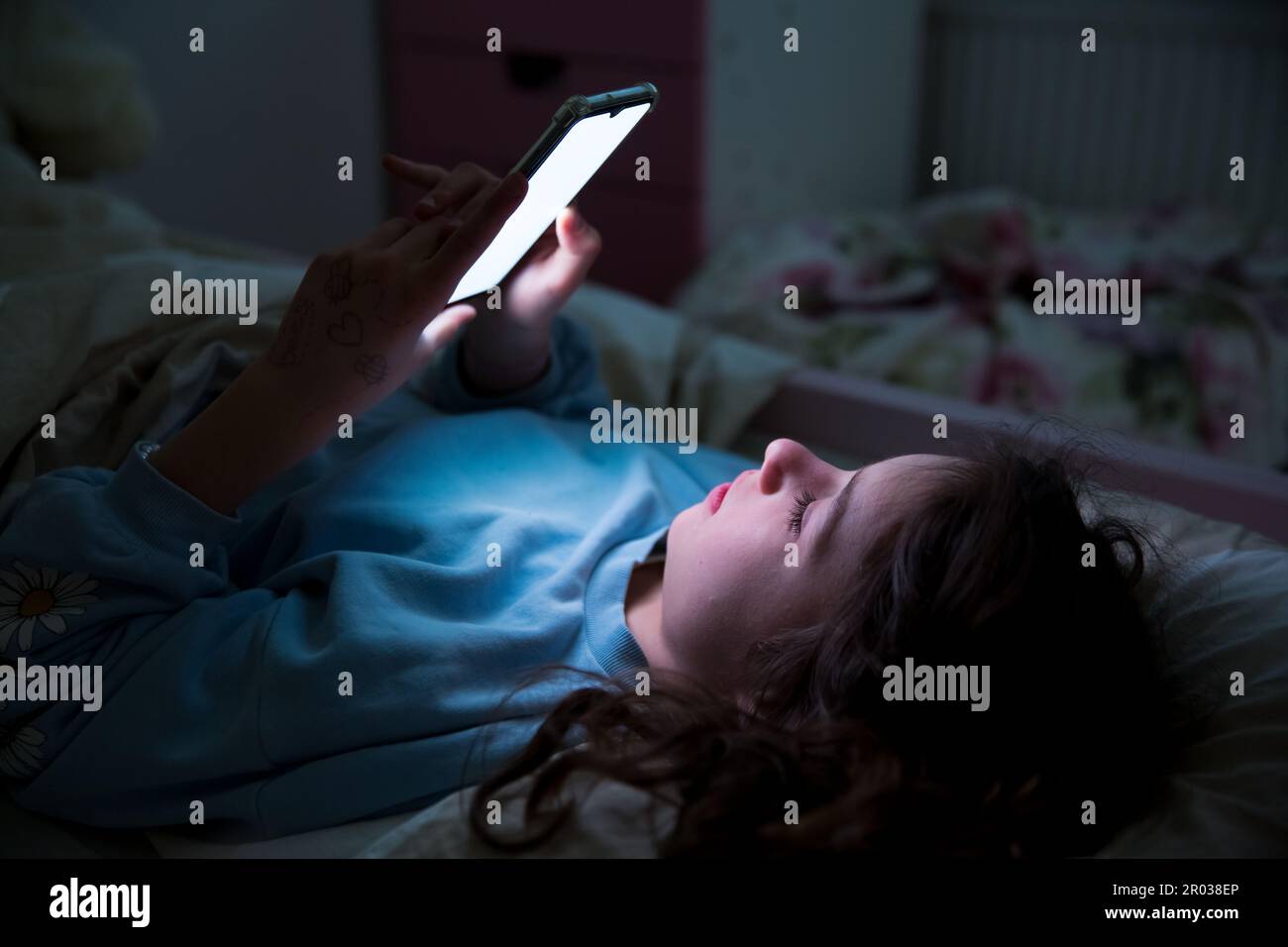 A child using smart phone lying in bed late at night, playing games ...