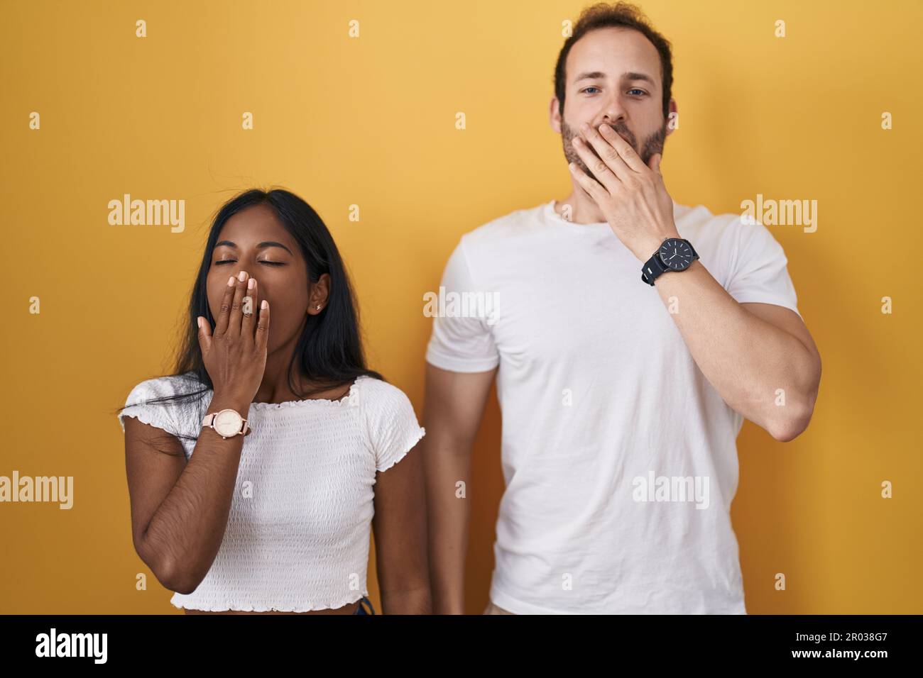 Interracial couple standing over yellow background bored yawning tired ...