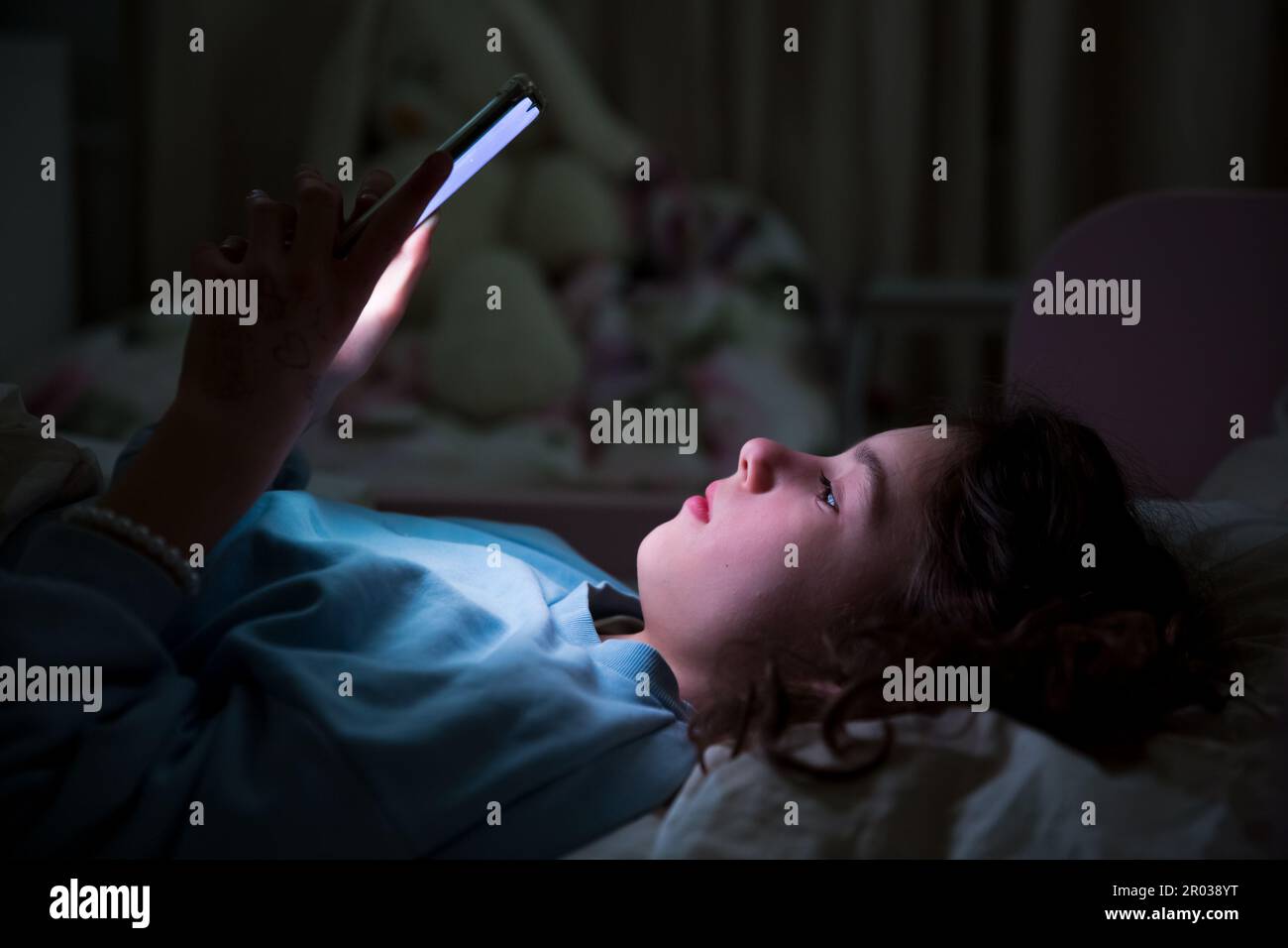 A child using smart phone lying in bed late at night, playing games ...
