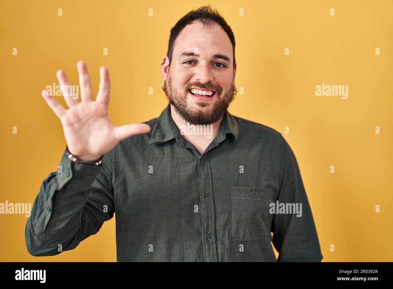 Plus size hispanic man with beard standing over yellow background ...