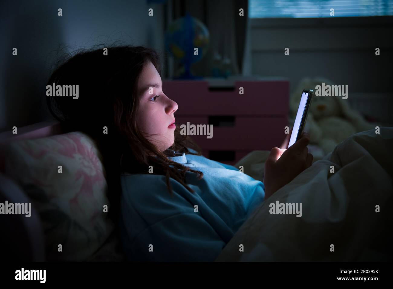 A child using smart phone lying in bed late at night, playing games ...