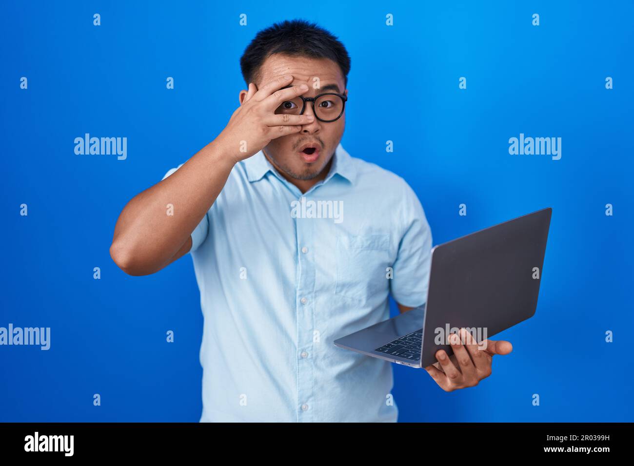Chinese young man using computer laptop peeking in shock covering face ...