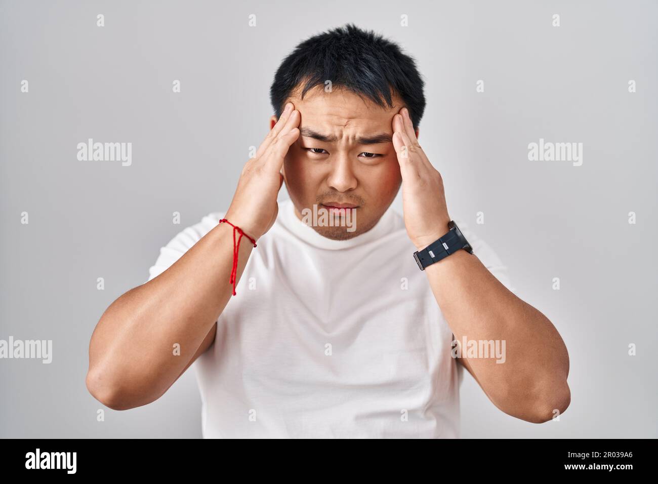 Young chinese man standing over white background with hand on head ...