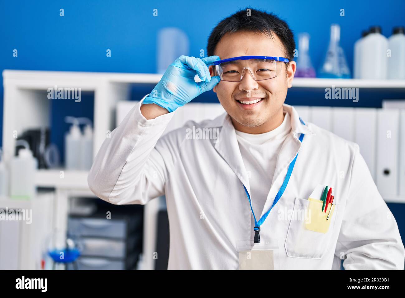 Young chinese man wearing scientist uniform standing at laboratory ...