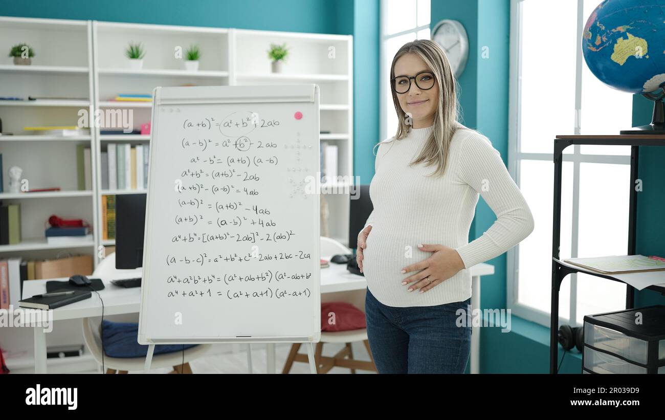 Young pregnant woman teacher teaching maths lesson touching belly at ...