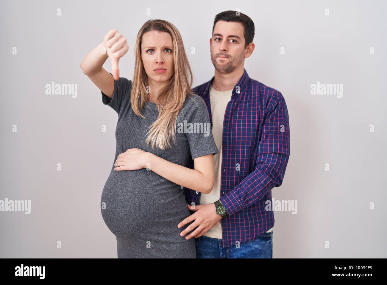 Young couple expecting a baby standing over white background looking ...