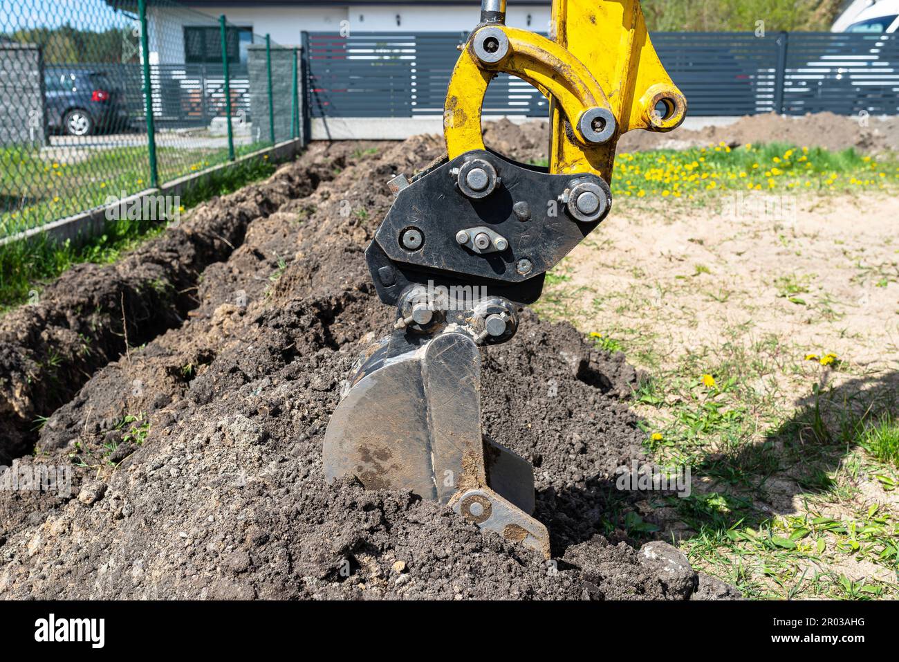 Mini digger digging a hole in the garden along the fence to the ...