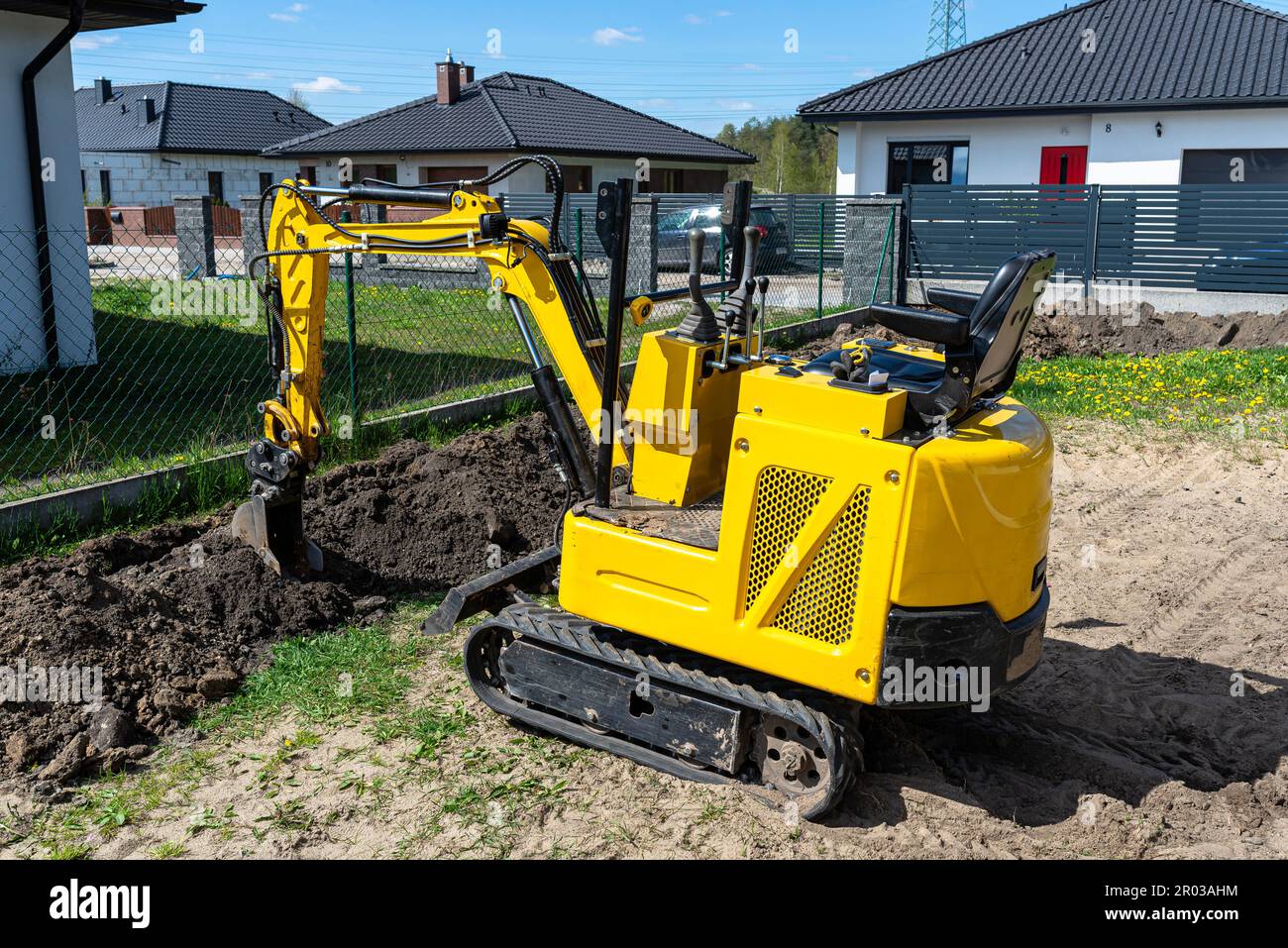 Mini digger digging a hole in the garden along the fence to the ...