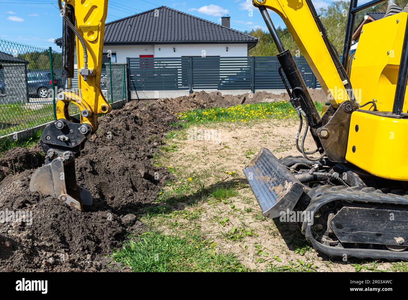 Mini digger digging a hole in the garden along the fence to the ...