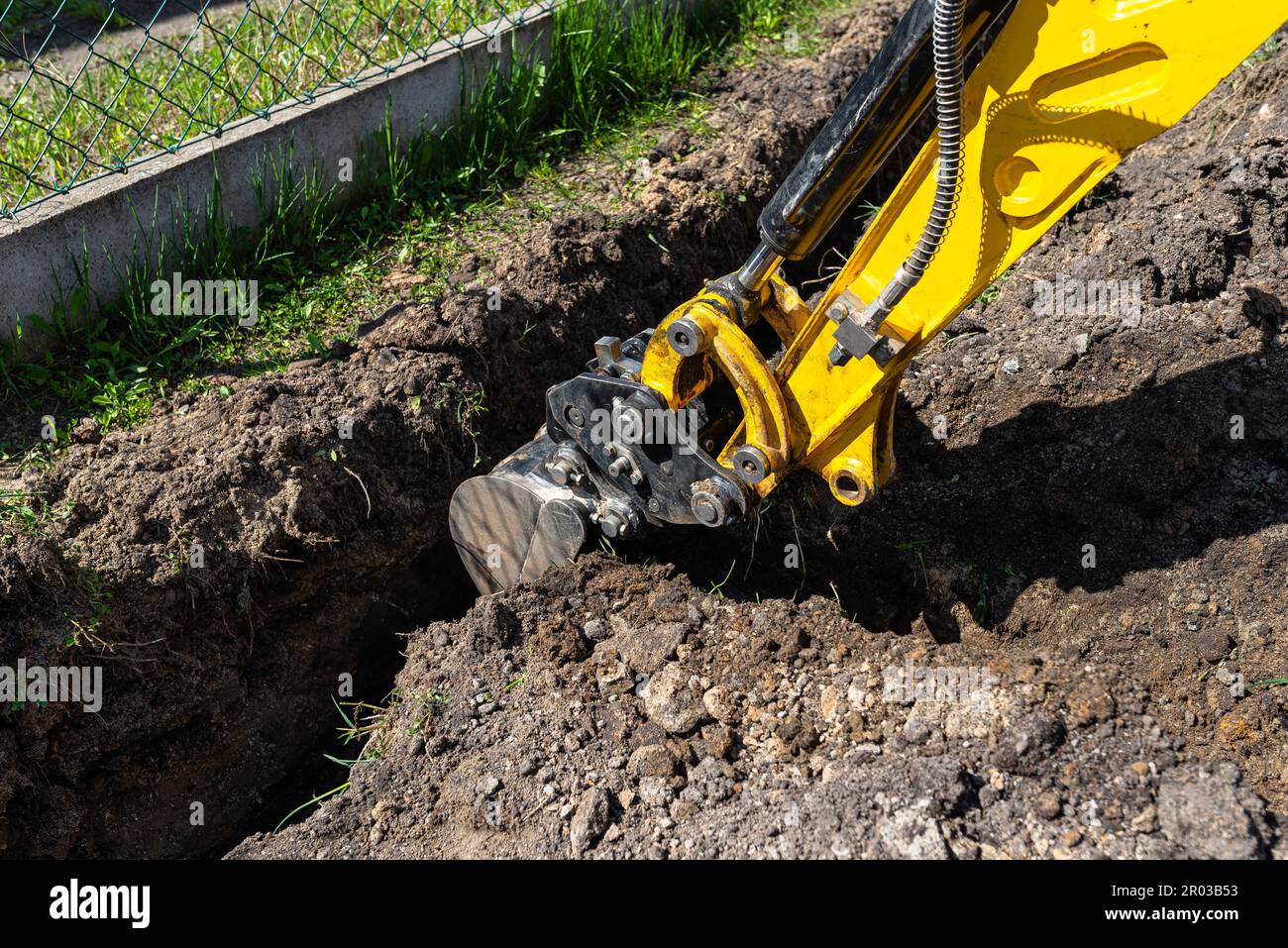 Mini digger digging a hole in the garden along the fence to the ...