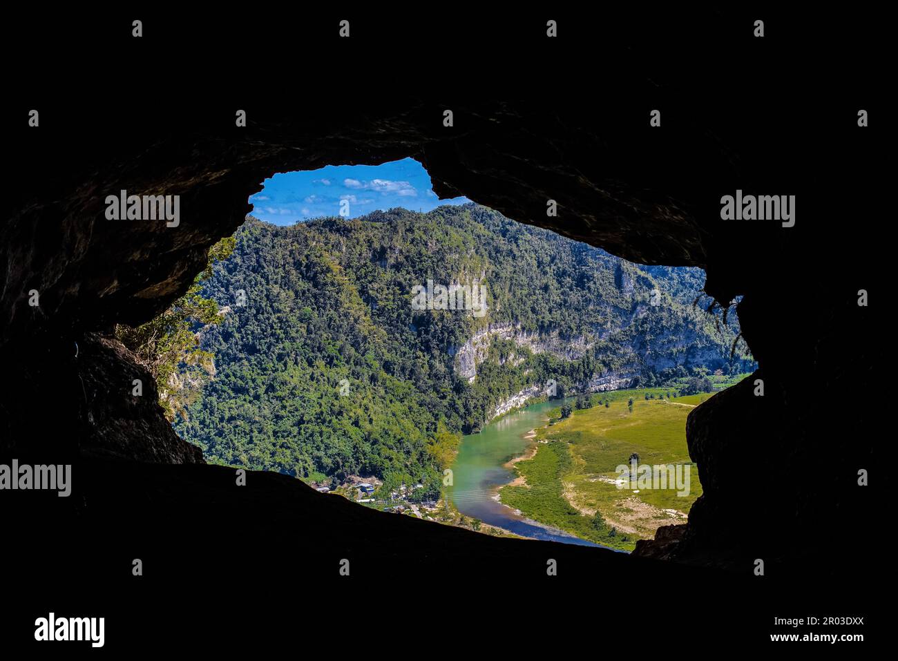 A close-up shot of a cave opening with a view of a river and lush trees ...