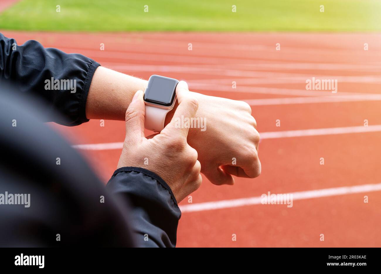 Digital watch on hand of athlete and running track on background ...
