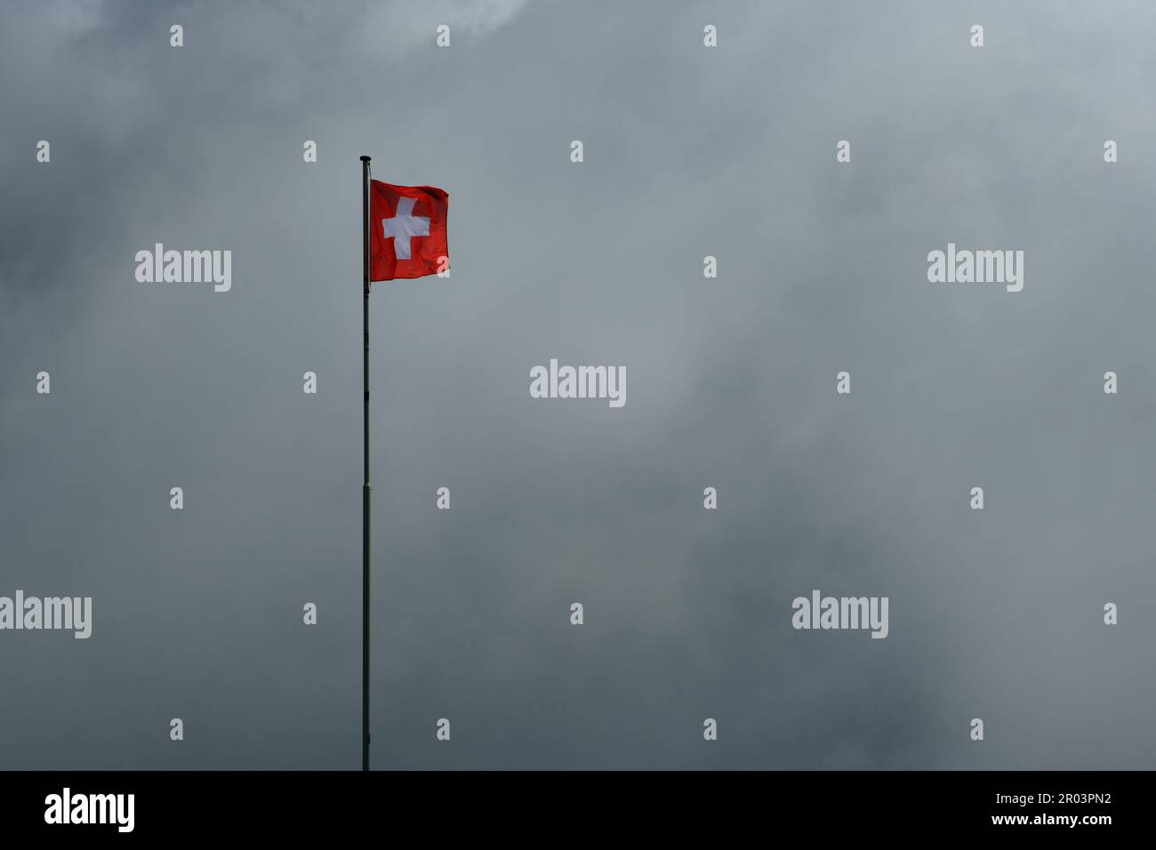 Swiss flag on flagpole waving in the wind against a cloudy background ...